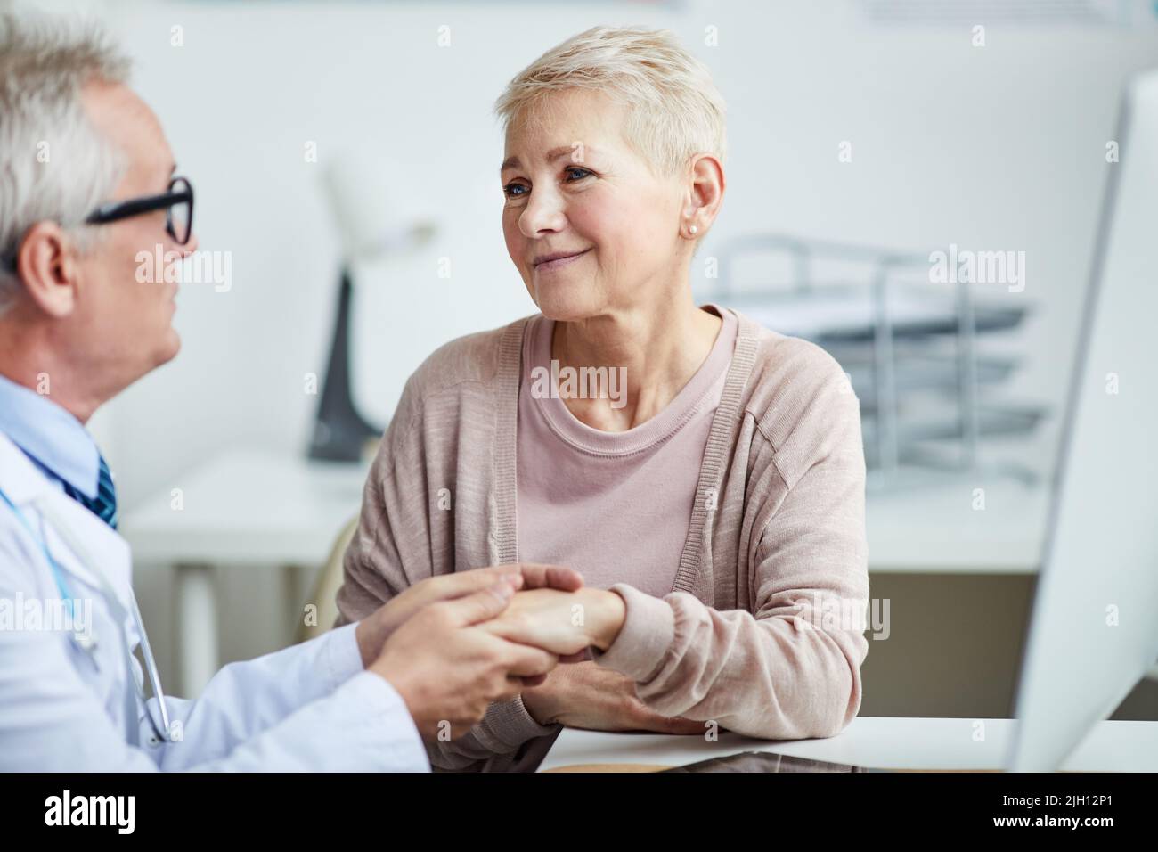 Professional male practitioner sitting at table and touching hands of ...