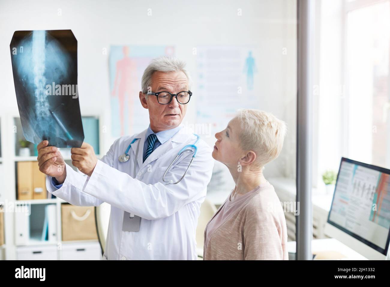Frowning handsome aged doctor in eyeglasses holding x-ray image against ...