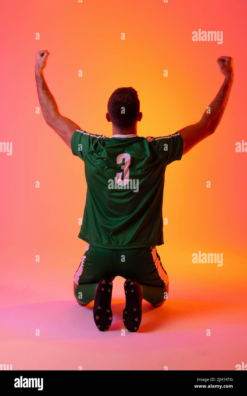 Caucasian male soccer player raising hands over neon pink lighting ...