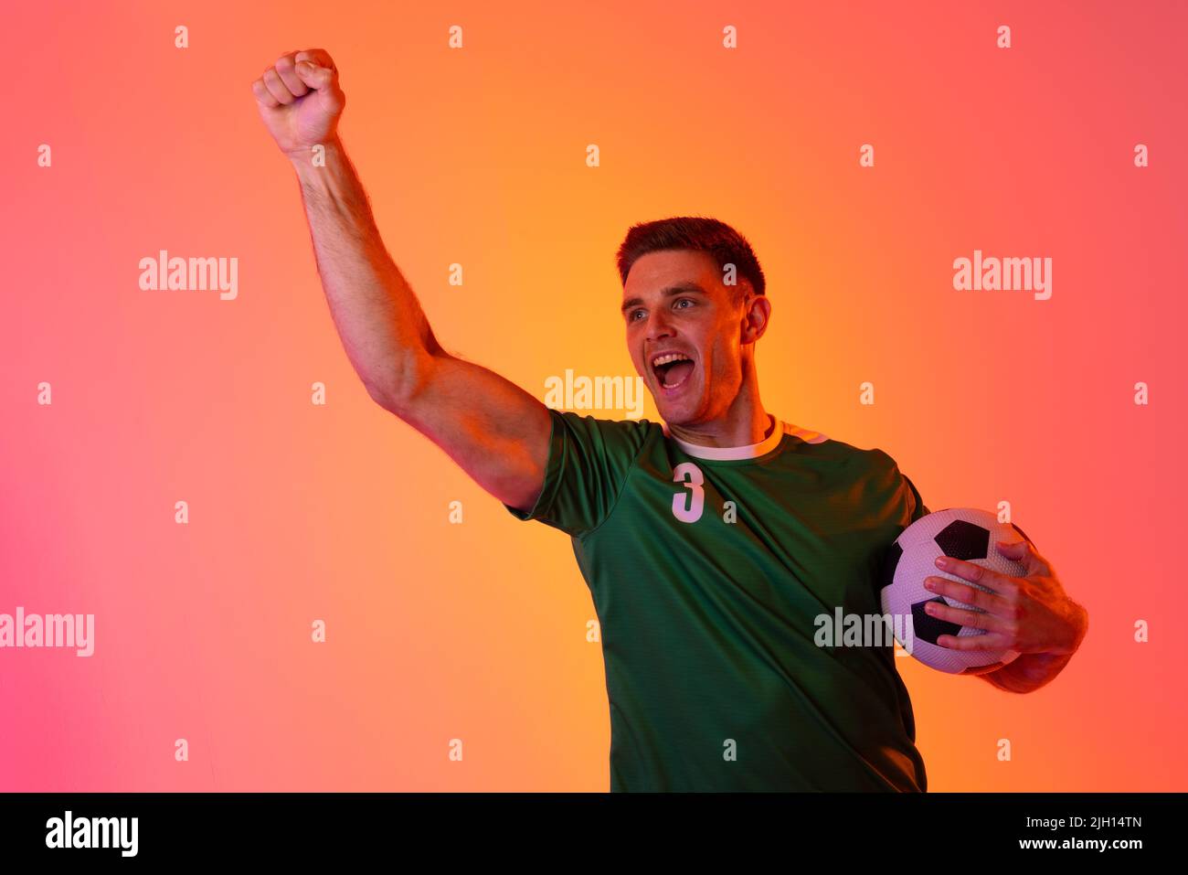 Happy caucasian male soccer player raising hand with football over neon ...