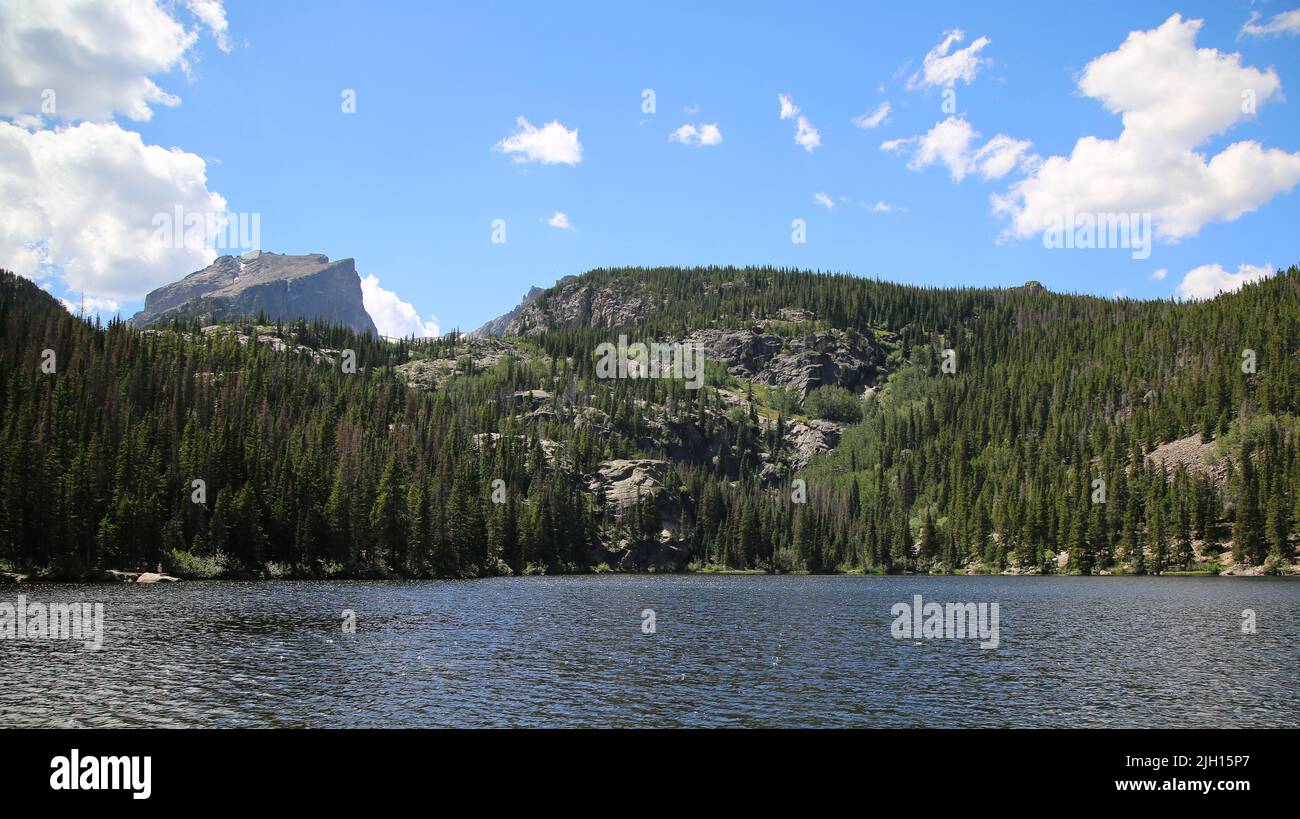 A scenic view of a lake against green pine forest on slope of Rocky ...