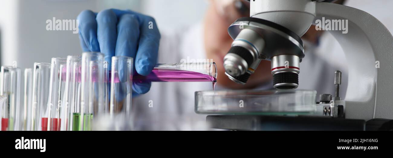Female scientist pouring pink sample liquid on glass container under ...