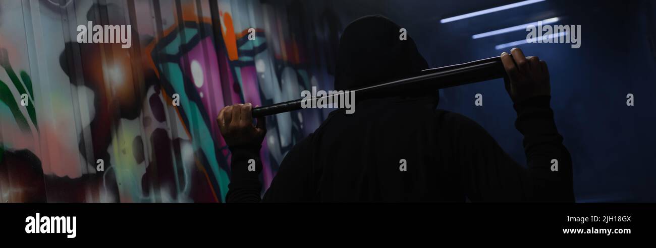 Back view of african american bandit in hoodie holding baseball bat in ...