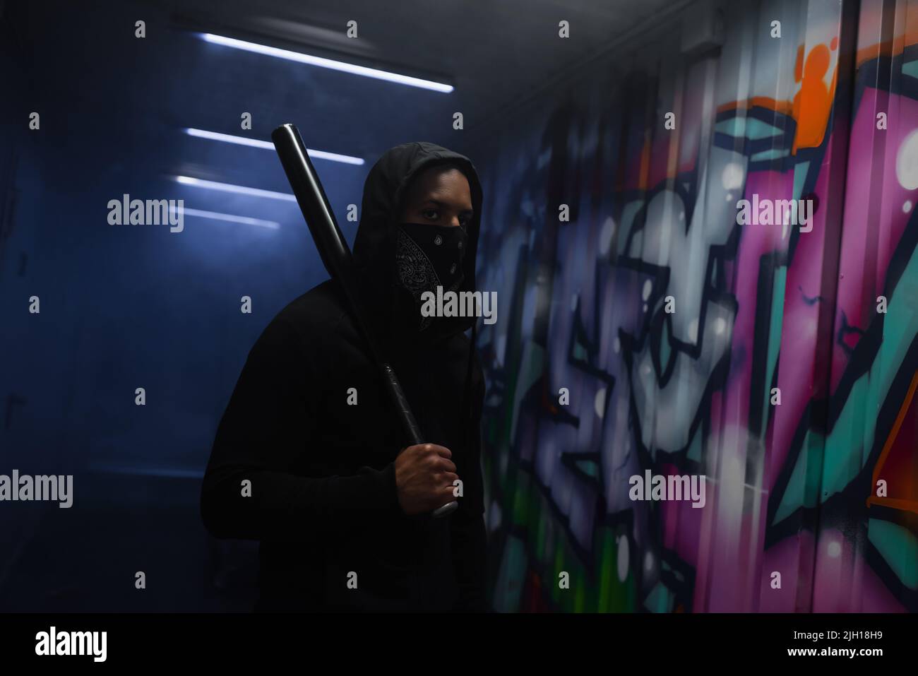 African american hooligan in mask holding baseball bat near graffiti ...