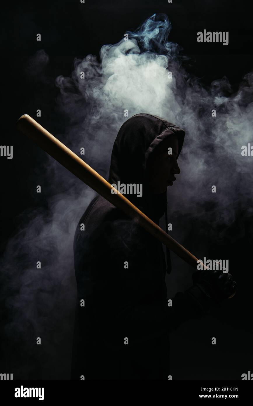 Side view of silhouette of hooligan with baseball bat on black ...