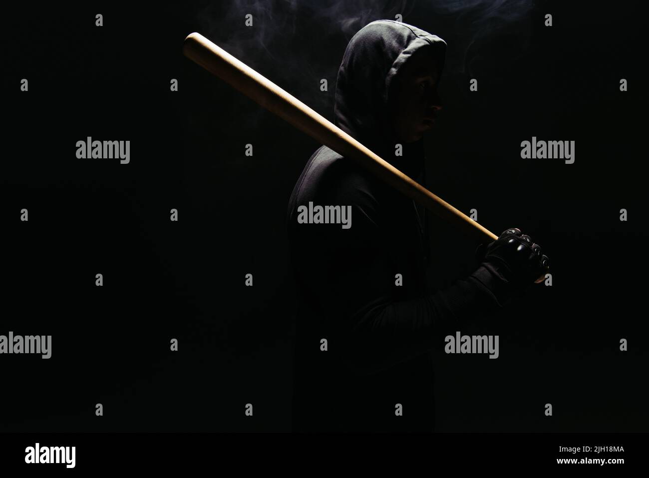 Silhouette of bandit in hoodie holding baseball bat on black background ...