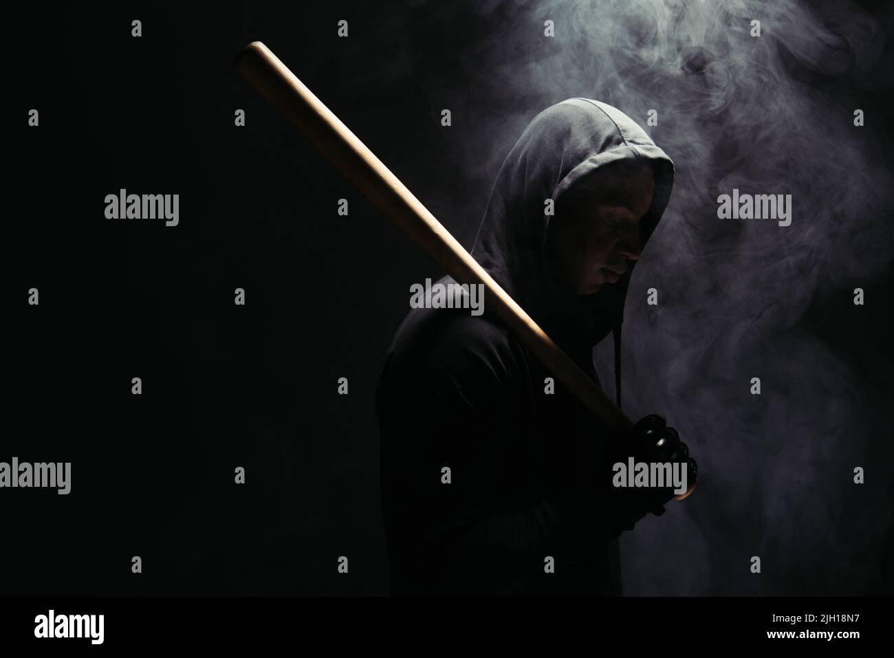 Side view of african american hooligan holding baseball bat in lighting ...