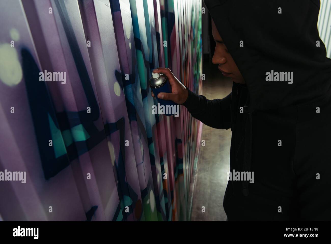 Side view of african american vandal with spray paint drawing graffiti ...