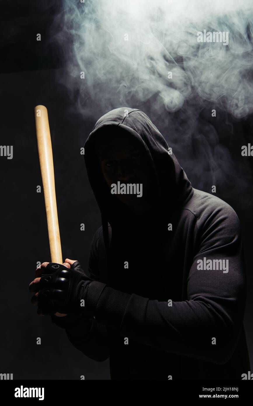 Silhouette of african american bandit in hood holding baseball bat on ...