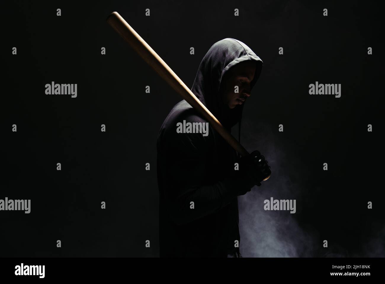 Side view of african american bandit in hood holding wooden baseball ...