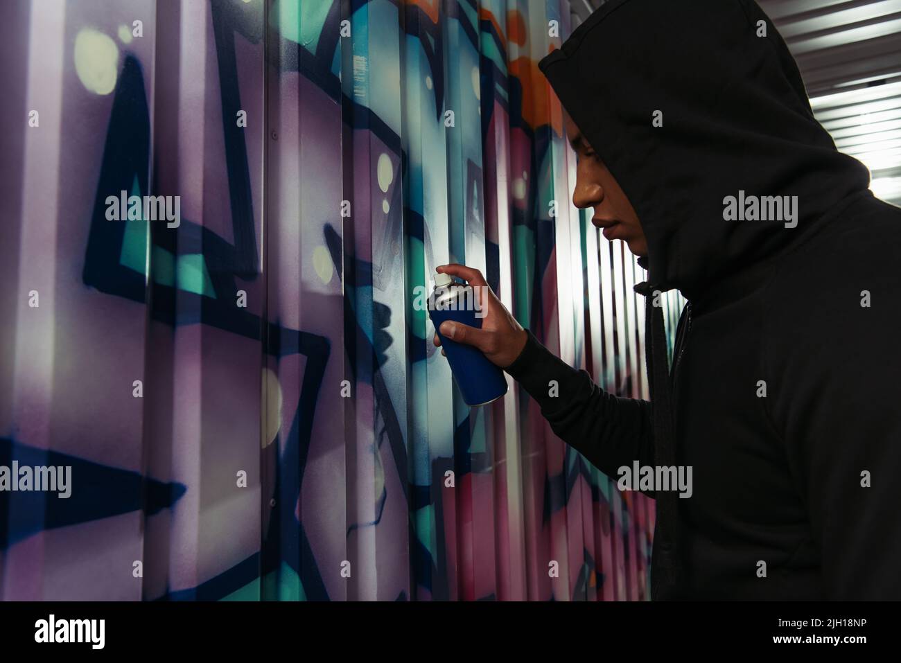Side view of african american vandal in hood drawing graffiti on wall ...