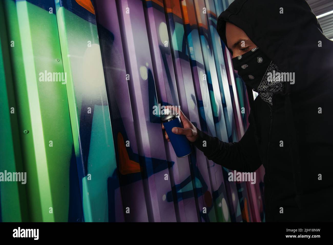 Side view of african american vandal with mask on face drawing graffiti ...
