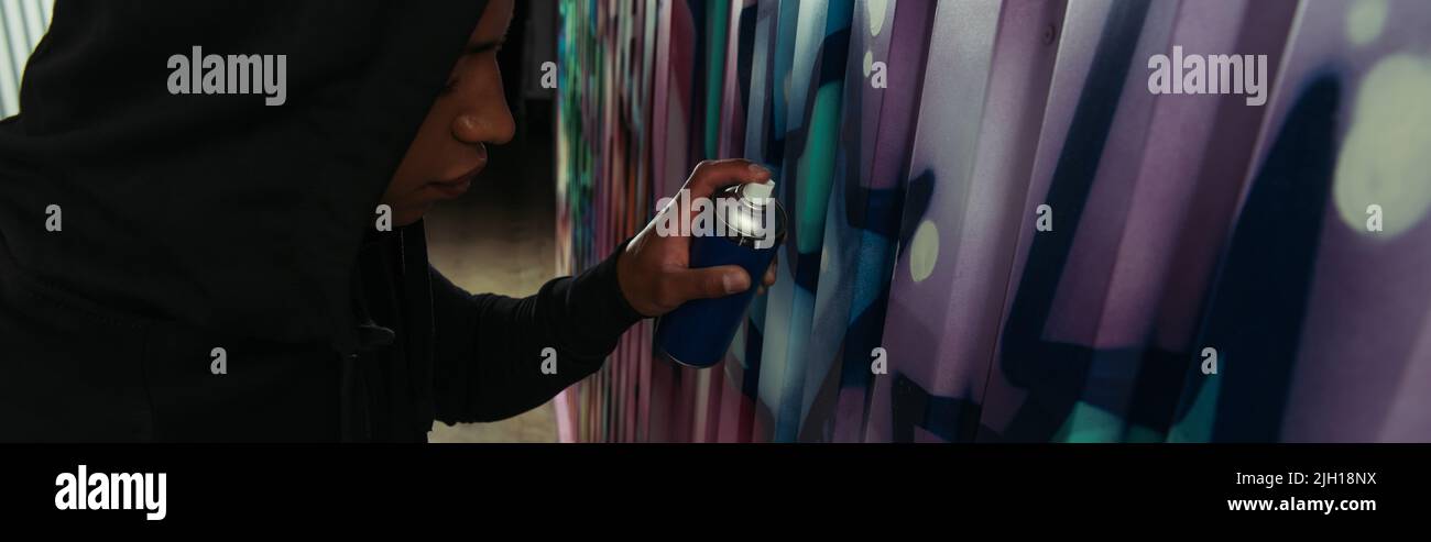 Side view of african american vandal drawing graffiti on wall, banner ...