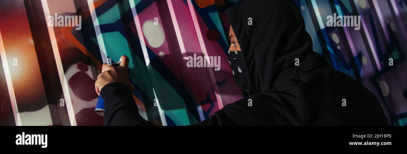 Side view of african american vandal in mask drawing graffiti on wall ...