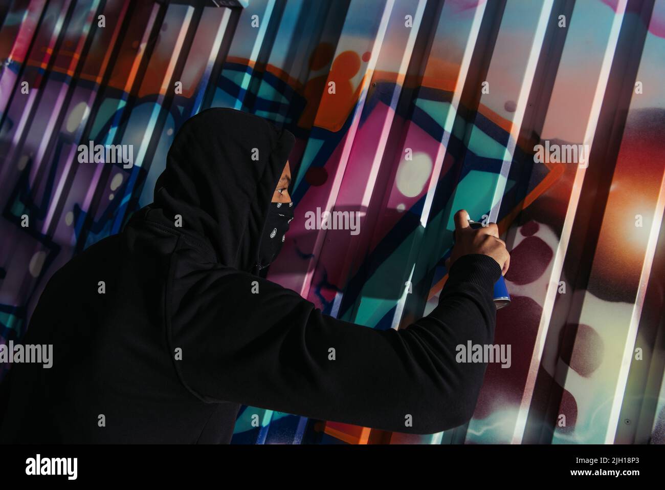 Side view of african american vandal drawing graffiti on wall outdoors ...