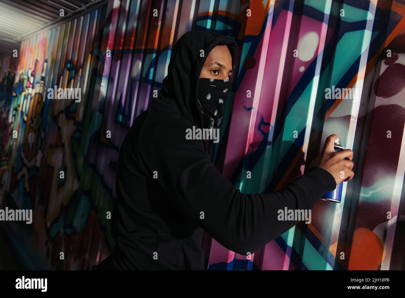 African american vandal with scarf on face drawing graffiti on wall ...