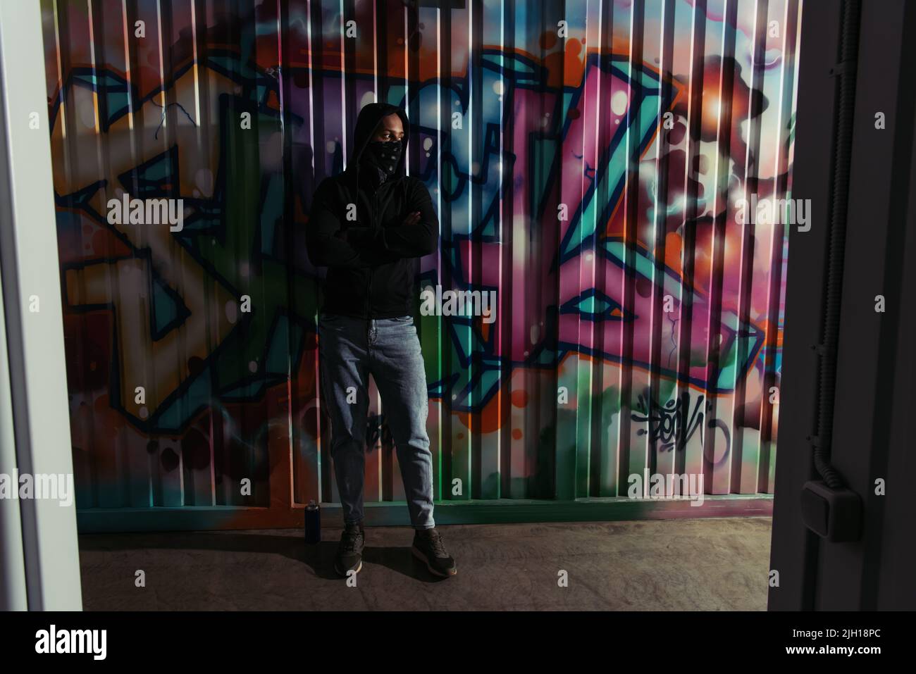 African american vandal with mask on face standing near graffiti on ...