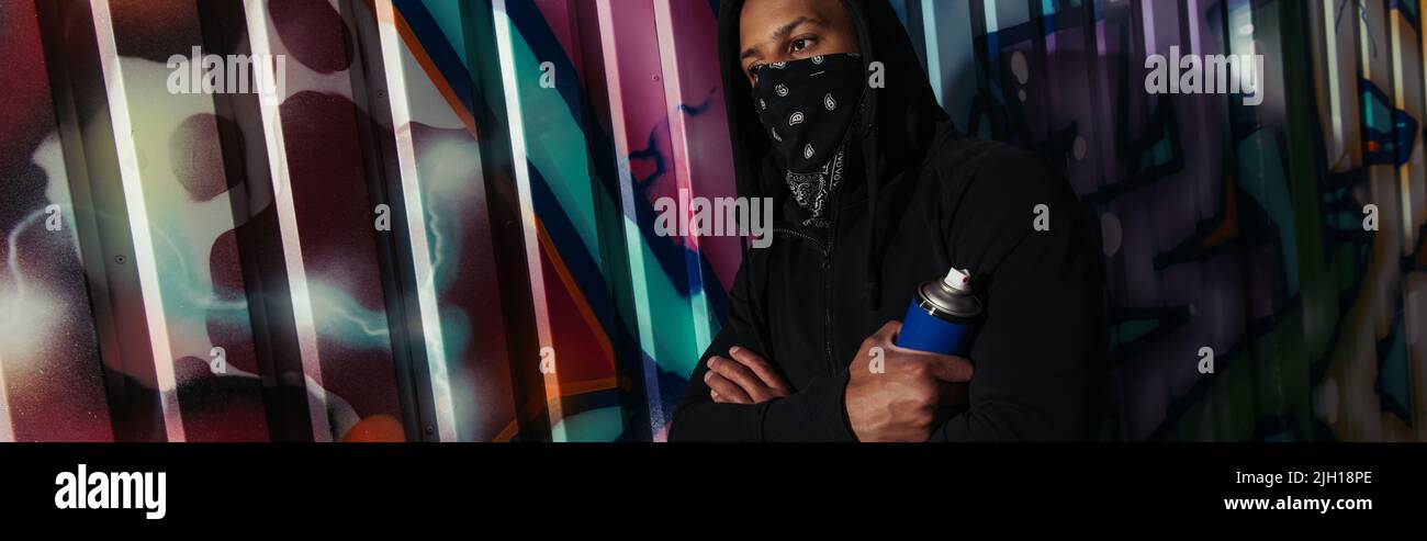 African american vandal with covered face holding spray paint near ...