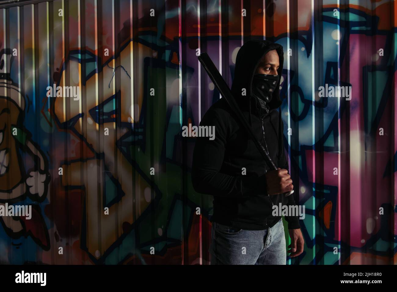 African american vandal with mask on face holding baseball bat near ...