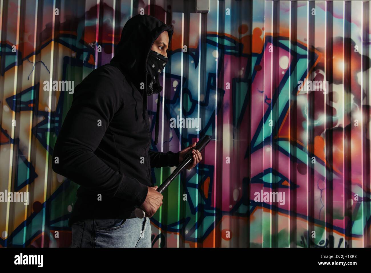 Side view of african american vandal holding baseball bat near graffiti ...