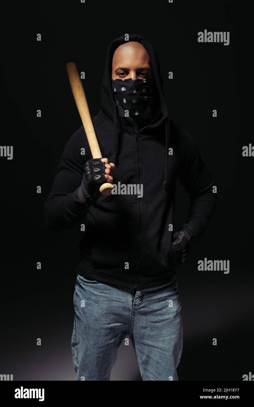 African american hooligan with scarf on face holding baseball bat on ...