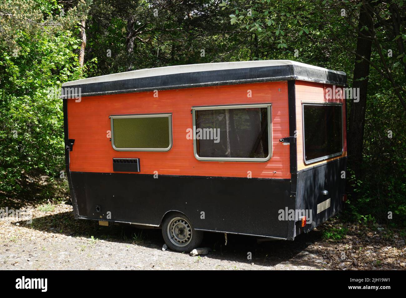 orange and black old caravan parked by the forest in the alps france ...