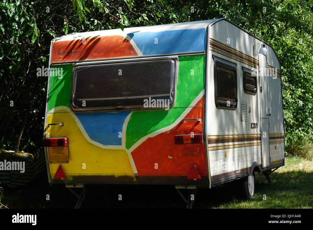 colorful painted caravan parked in the shade by some trees in france ...
