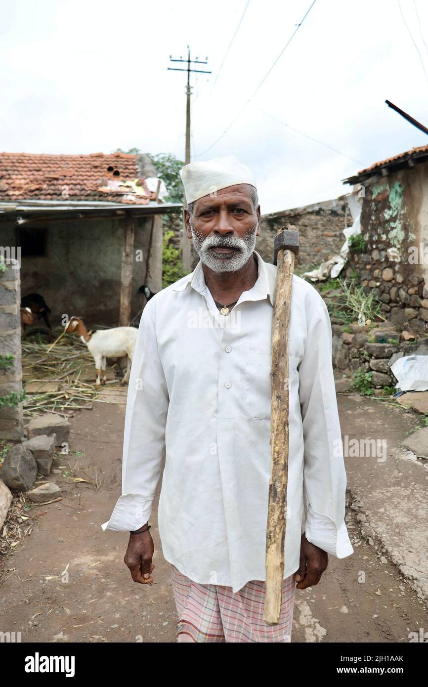 A selective focus of an old Indian farmer holding an axe on his ...