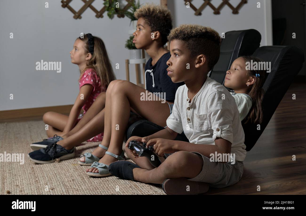 Four pretty multi-national kids playing gaming console at home ...