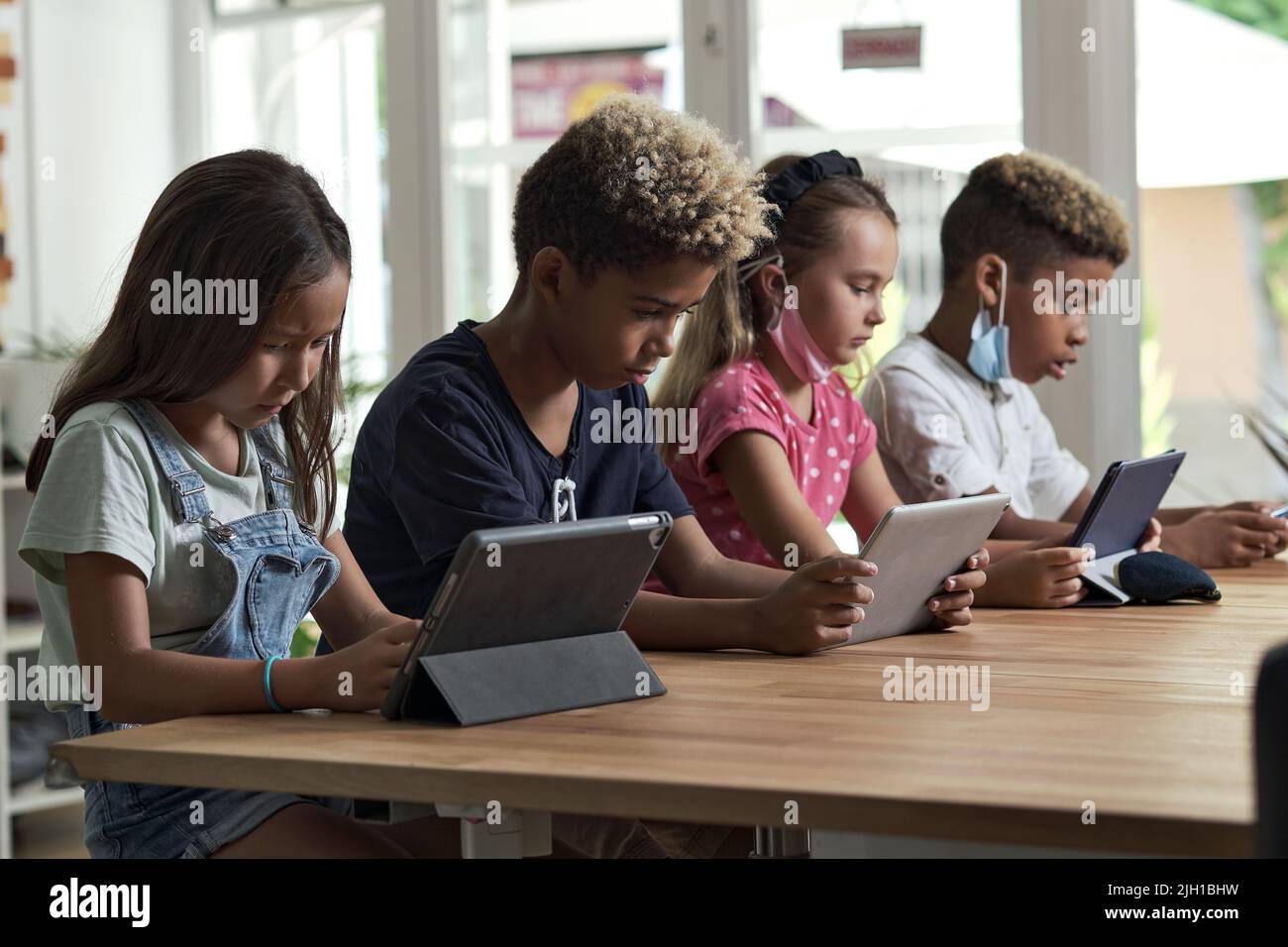 Four pretty multi-national kids playing at tablet at home - virtual ...