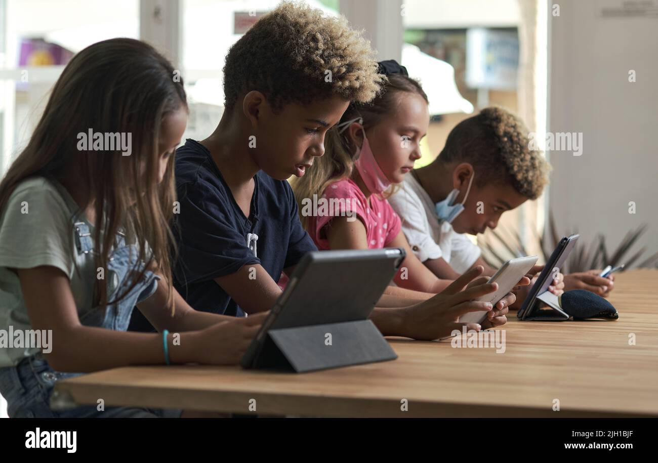 Four pretty multi-national kids playing at tablet at home - virtual ...
