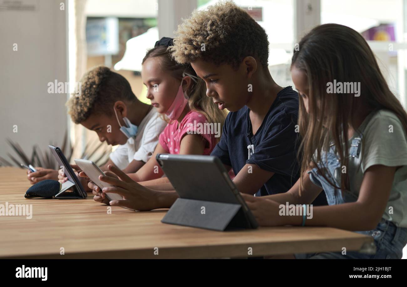 Four pretty multi-national kids playing at tablet at home - virtual ...