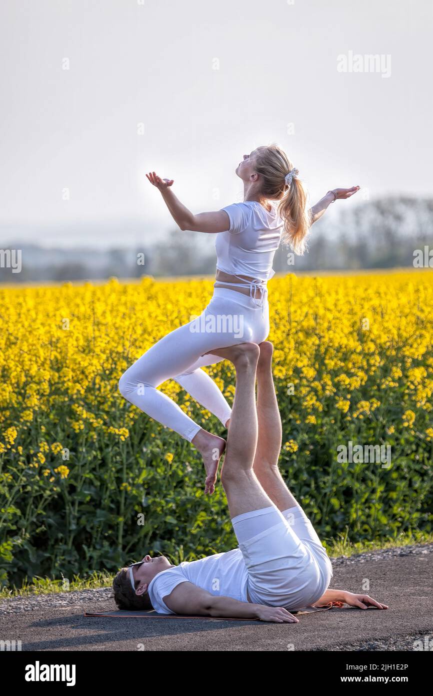Beautiful young couple doing acro yoga on the bike path. Man lying on road and balancing woman ...