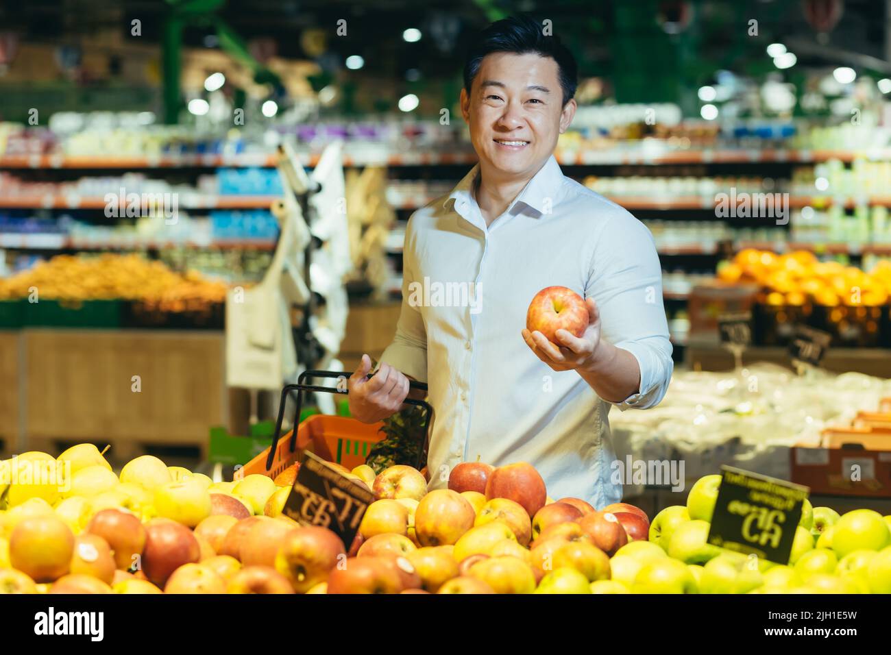Portrait of Asian supermarket buyer, man chooses apple fruit and put to ...