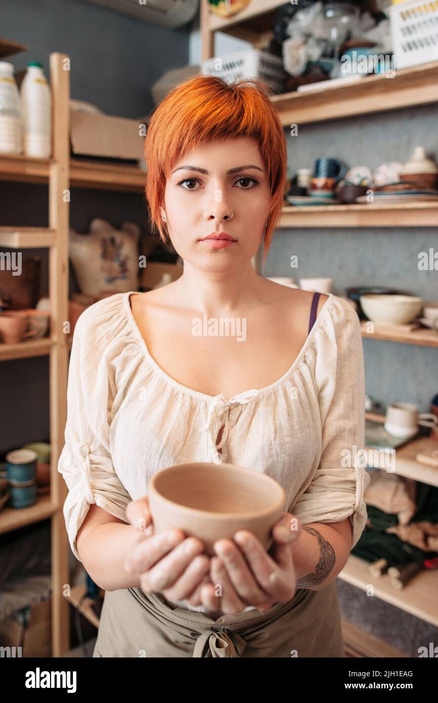 Female potter holding clay bowl at studio. Woman craftsman shows ...