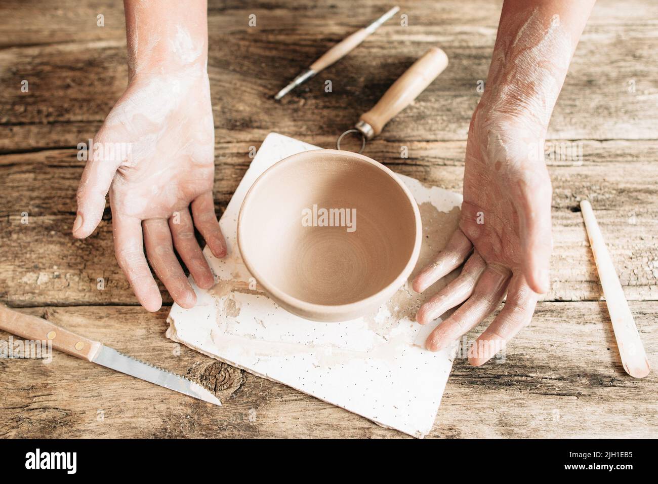Craftsman hands with pottery and tools on wood close-up. Newcomer at ...