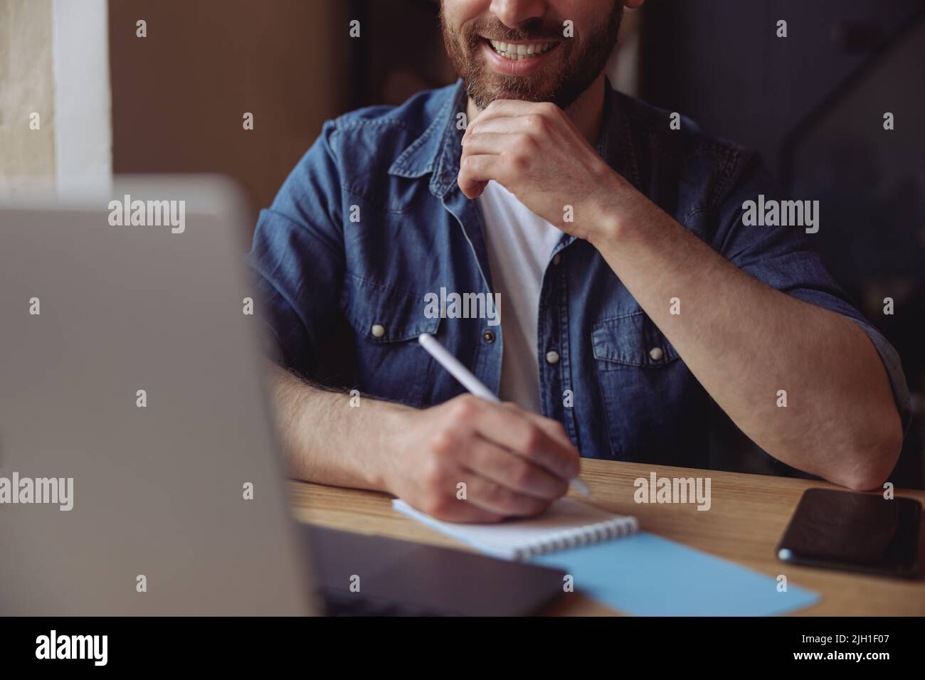 Hands of cheerful man with pen while taking notes at laptop and smiling ...