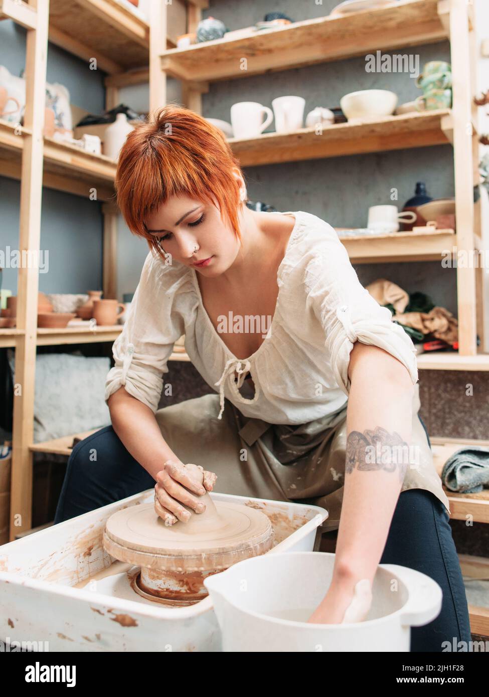 Young female potter working with clay at studio. Front view on red ...