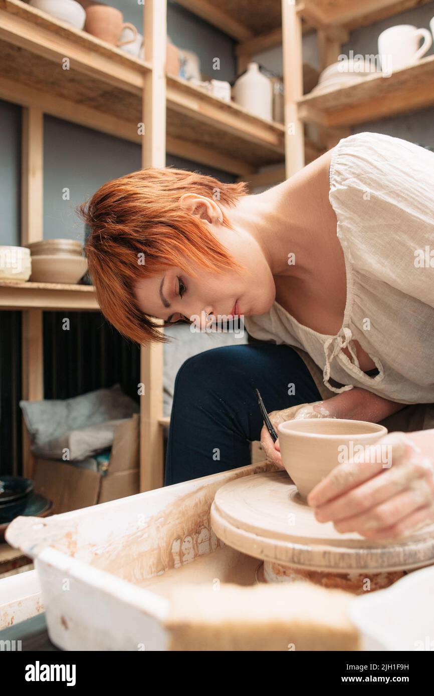 Intently working on pottery wheel craftswoman. Crockery making process ...