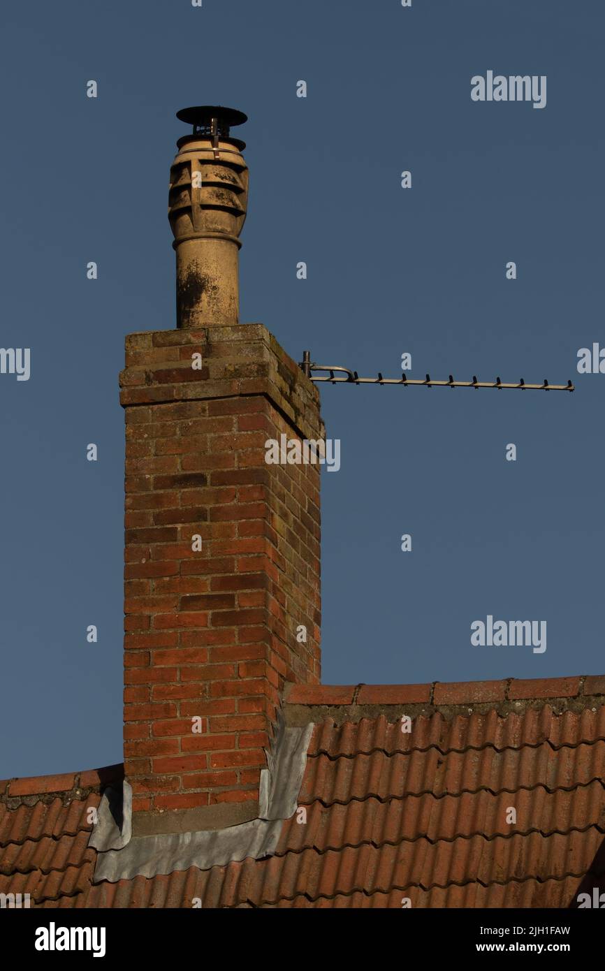 A vertical shot of tall chimney pot on red brick chimney stack and roof ...
