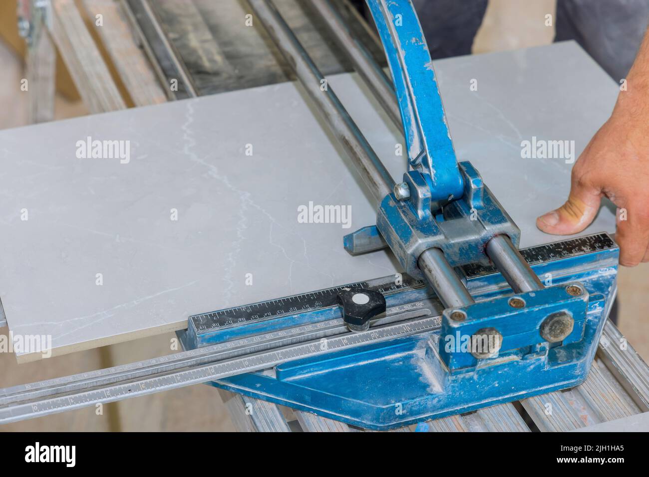 On a ceramic tile floor, a construction worker uses a manual tool to ...