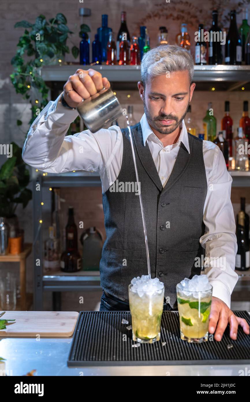 Barman making cocktail Mojito in night club adding ingredients and ...