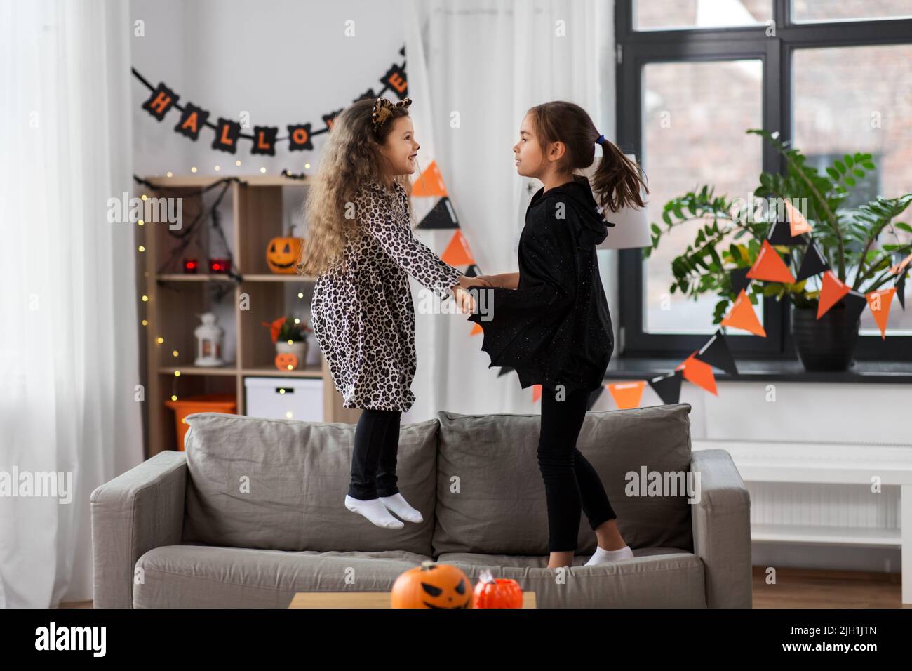 girls in halloween costumes jumping on sofa Stock Photo - Alamy