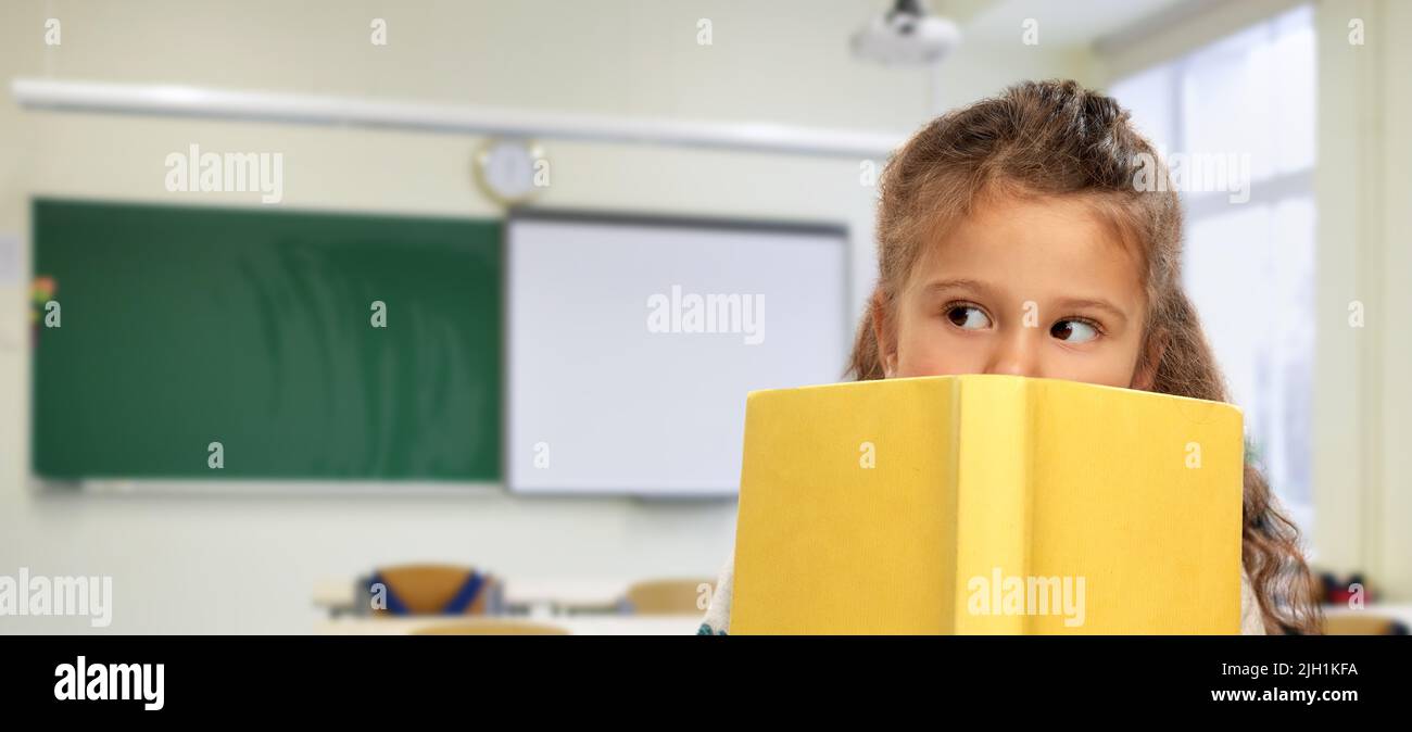 little girl hiding behind yellow book at school Stock Photo - Alamy