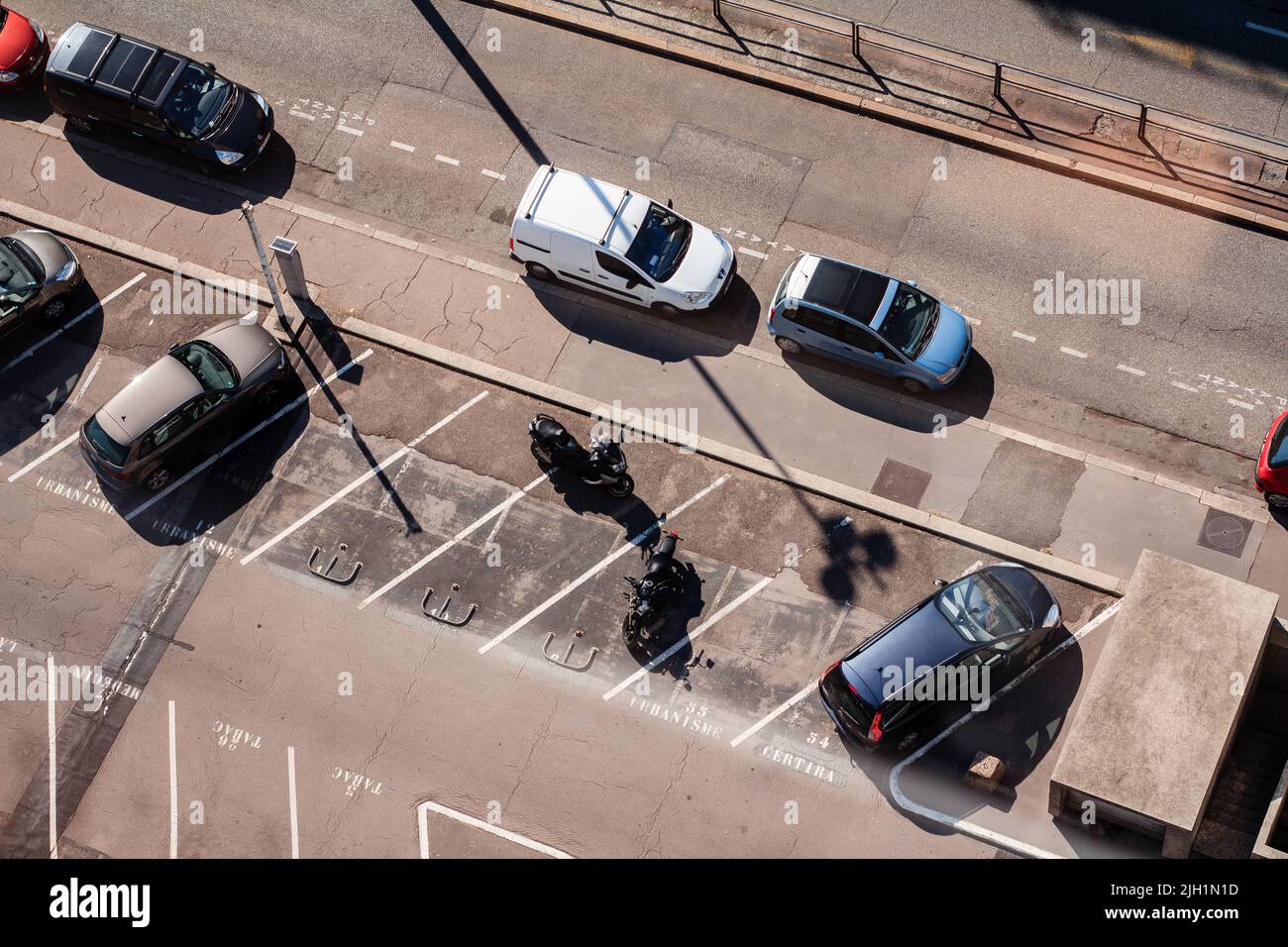 A rooftop view of cars and motorbikes parked in a parking lot and along ...