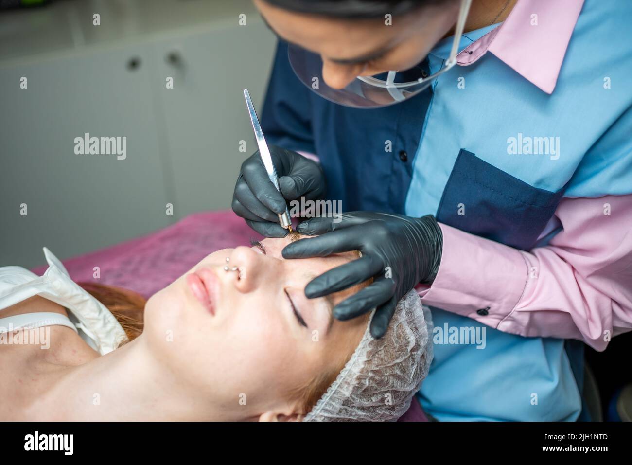 Procedure of eyebrow microblading. A master in black gloves is doing a ...