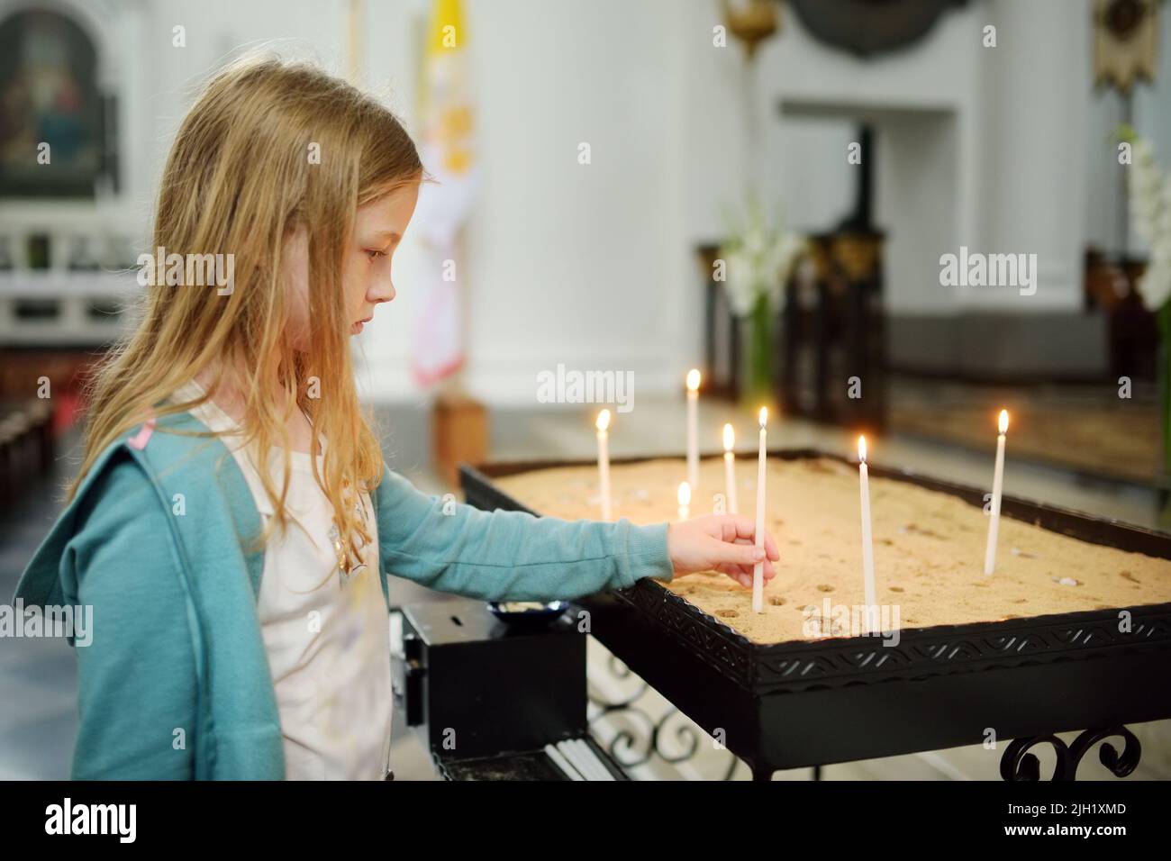 Cute little girl lighting a candle in a church. A child holding small ...