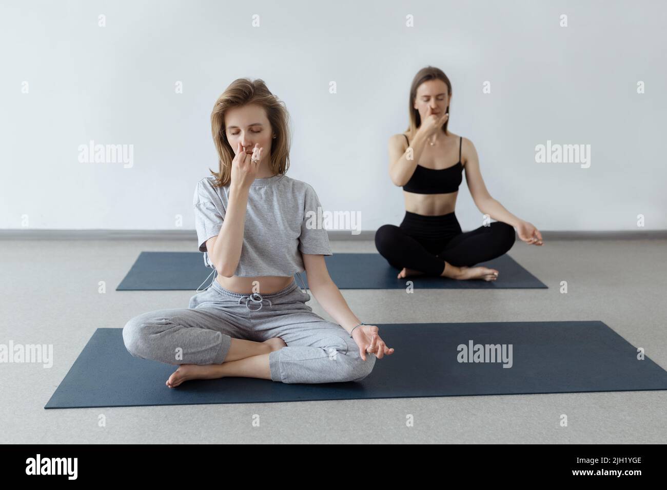 Two athletic attractive girls sit in lotus position on yoga mat indoors ...