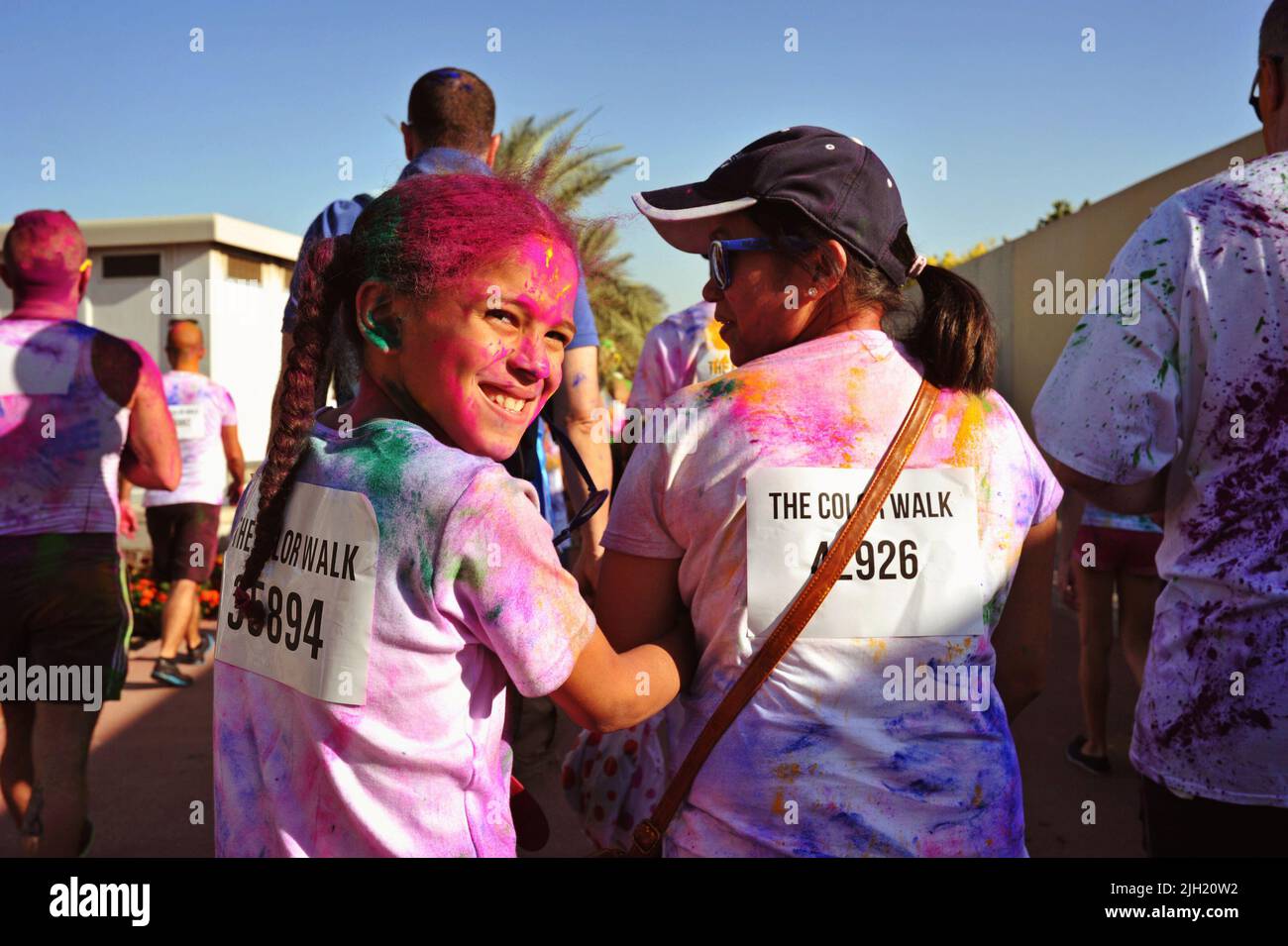 Young girl with long braids covered in colored powder looks behind with ...