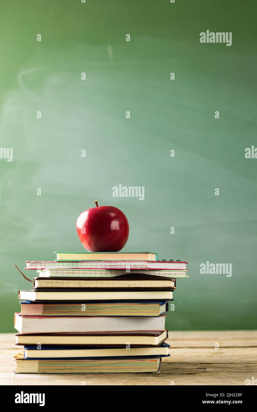 Image of books, notebook and apple on wooden table over black board ...